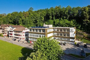 Hotel de vários andares com um átrio central, rodeado por vegetação e outros edifícios.