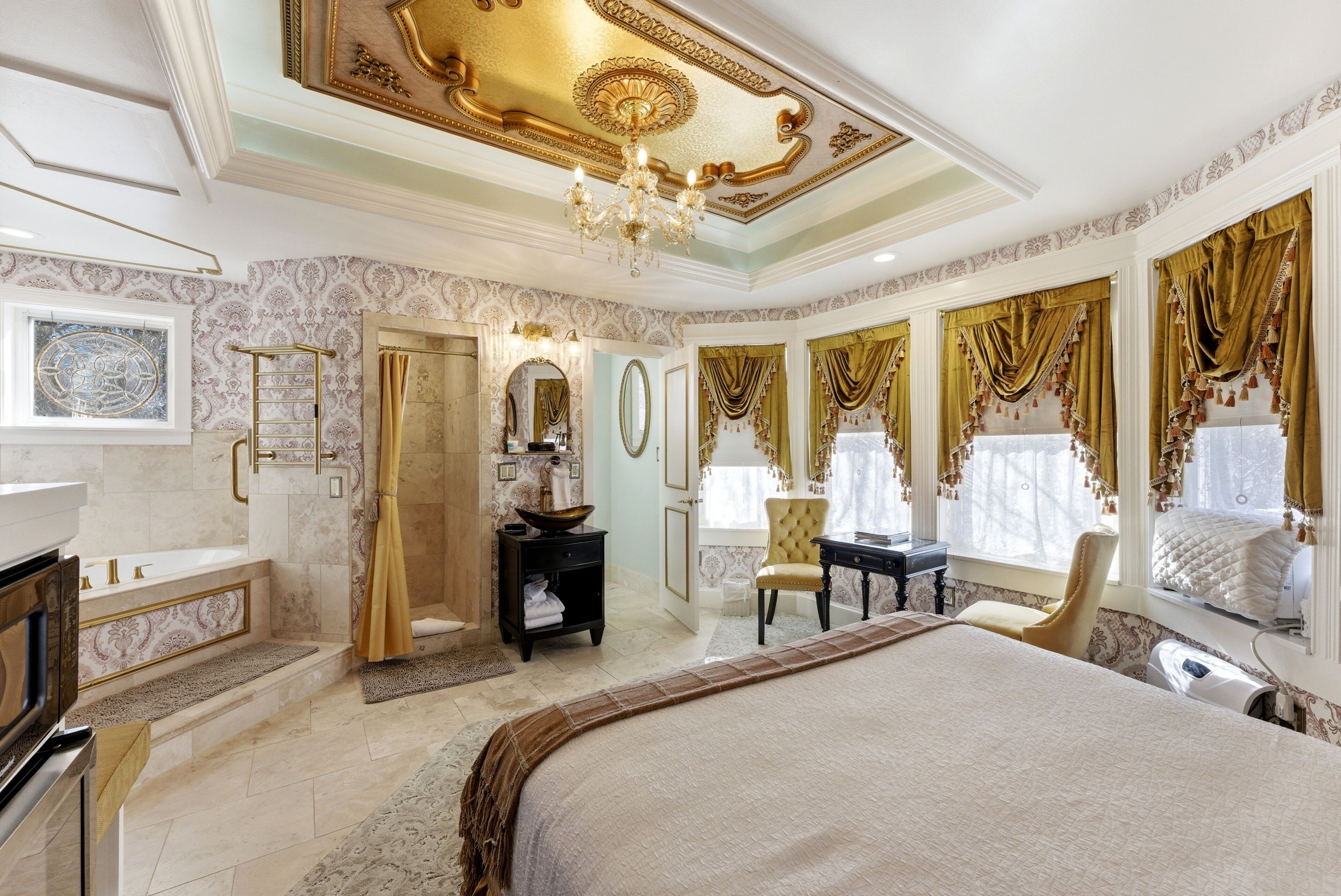 Um quarto luxuoso com uma cama grande, uma toucador com espelho, um lustre e vista para o exterior.