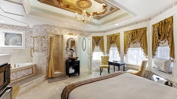 Um quarto luxuoso com uma cama grande, uma toucador com espelho, um lustre e vista para o exterior.