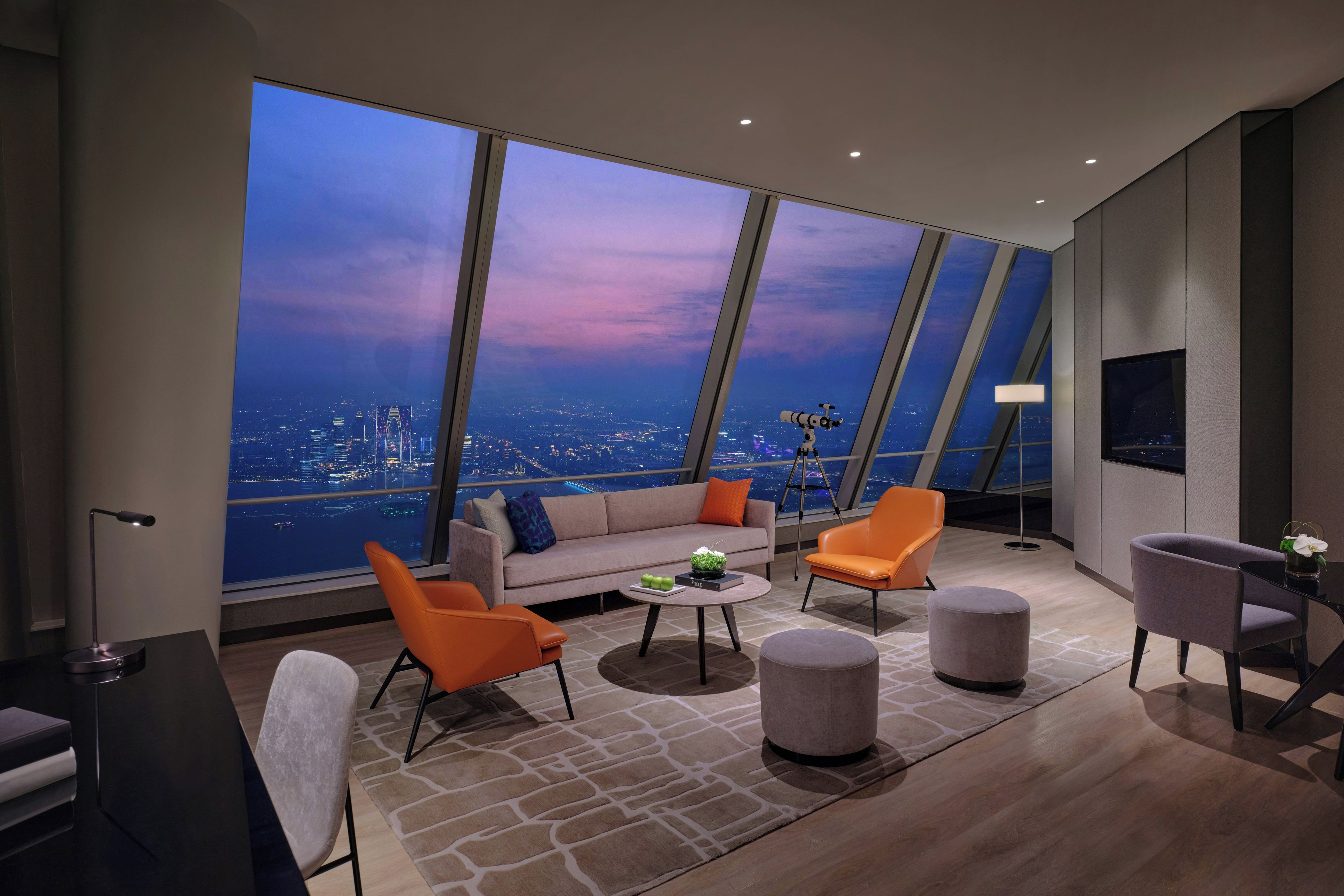 Sala de estar moderna com vista para a cidade, um sofá, duas poltronas, uma mesa de centro e um abajur.