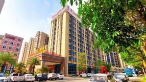 Um hotel com vários andares e uma entrada imponente, com vários carros estacionados e áreas verdes ao redor.