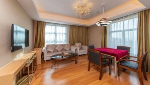 Uma sala de estar moderna com sofá, mesa de centro, mesa de jantar com cadeiras, TV fixada na parede e grandes janelas com cortinas.