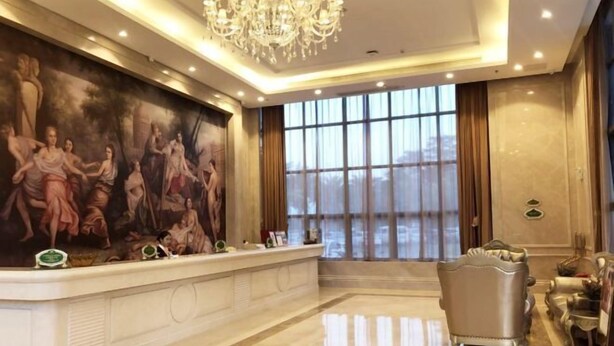 Um hall amplo com uma receção de mármore, um grande mural clássico e um imponente candelabro.
