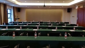 Uma sala de conferências com fileiras de mesas, cada uma com uma garrafa de água e um bloco de notas.