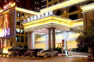 Entrada de hotel com toldo grande, vários andares e carros estacionados.