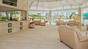 Um espaço interno amplo com sofás bege e uma piscina ao fundo.