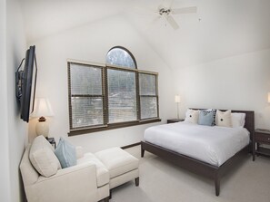Quarto com cama, mesa de cabeceira, abajur, ventoinha no teto e janela com persianas.