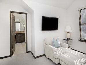 Uma sala de estar moderna com televisão de tela plana, sofá, abajur e janela com persianas.