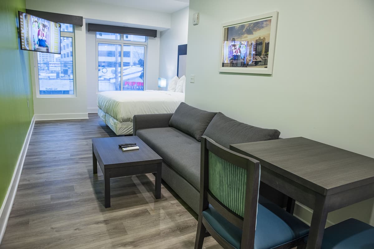 Quarto de hotel com cama, sofá, mesa de jantar e televisão na parede.