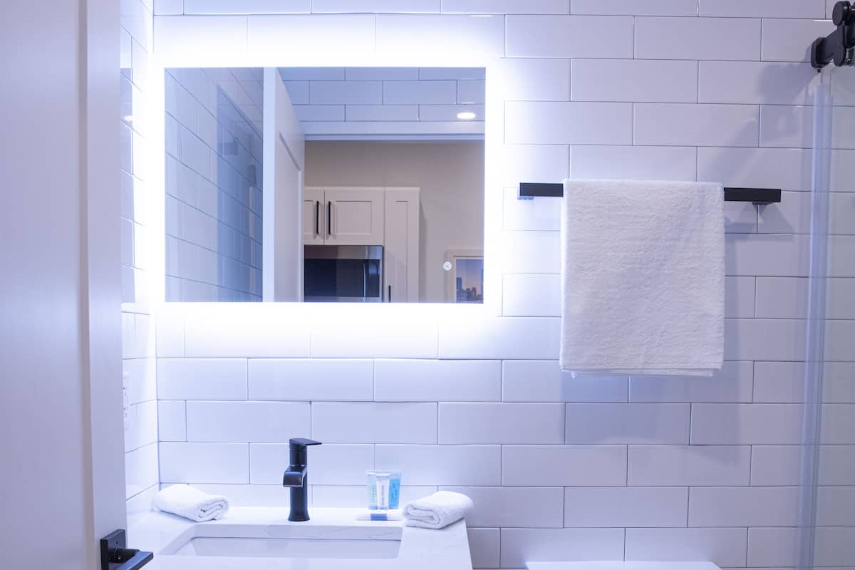 Casa de banho moderna com lavatório branco, espelho e sanita. Toalhas e chuveiro são visíveis.