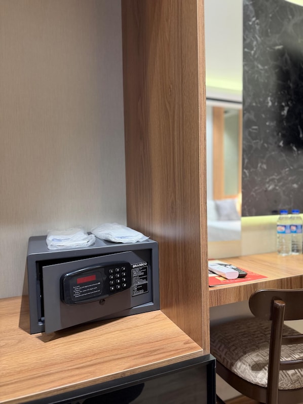 Quarto com micro-ondas sobre uma mesa de madeira, uma cadeira, controle remoto e garrafas de água na mesa.