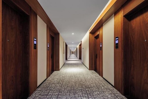 Um corredor de hotel comprido e estreito, com portas de madeira em ambos os lados e um carpete estampado.