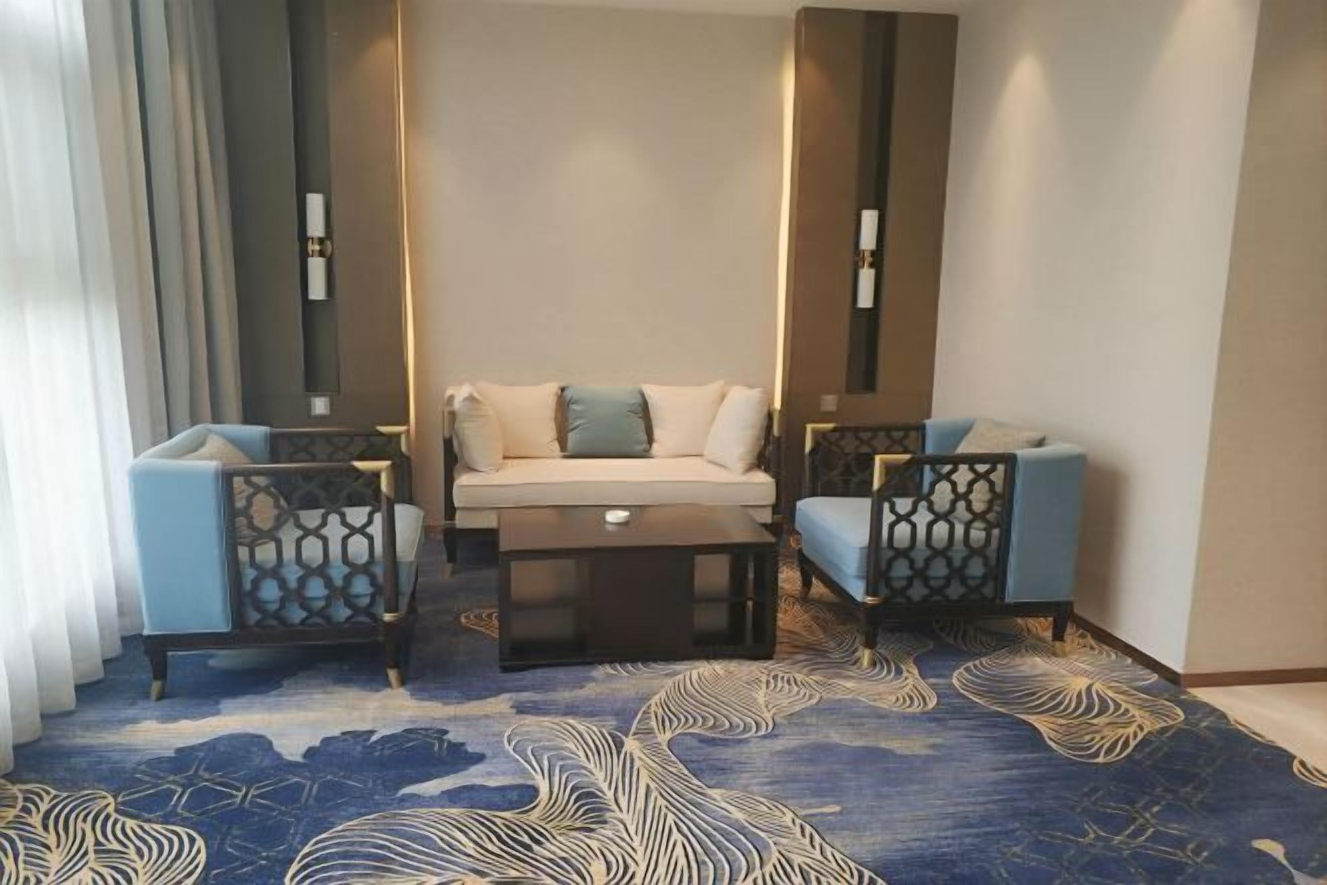 Quarto com sofá, duas poltronas, mesa de centro e carpete estampado.