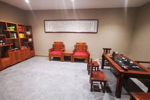 Quarto com mesa de futebol de mesa, duas cadeiras de madeira com almofadas vermelhas, uma estante e uma obra de caligrafia emoldurada na parede.