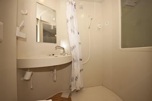 Casa de banho com lavatório, espelho, chuveiro e dispensador de papel higiénico.