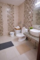 Casa de banho com azulejos estampados, sanita, bidé, lavatório e uma pequena planta.