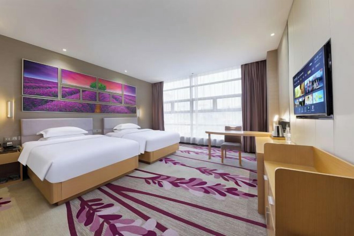 Quarto de hotel com duas camas, uma escrivaninha, televisão e uma janela grande.