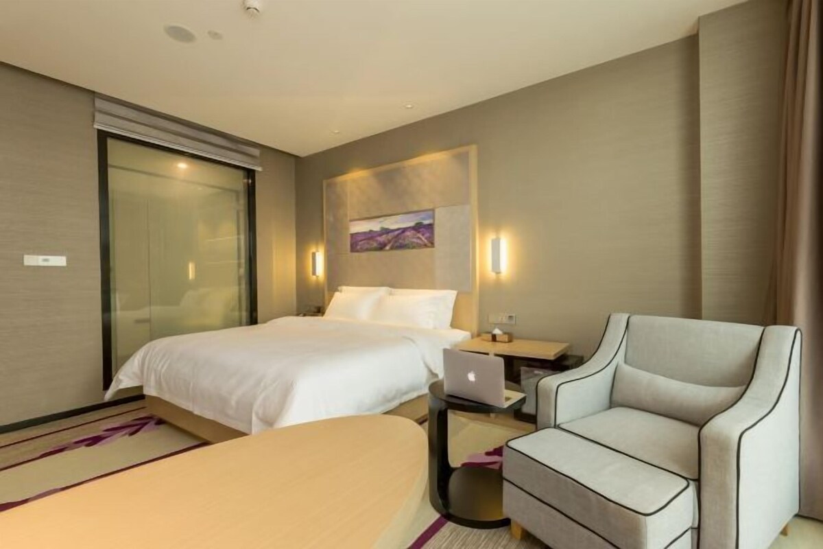 Quarto de hotel com cama, escrivaninha com laptop, cadeira e quadro na parede.