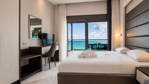 Quarto de hotel com cama, escrivaninha, poltrona, televisão e vista para o mar.