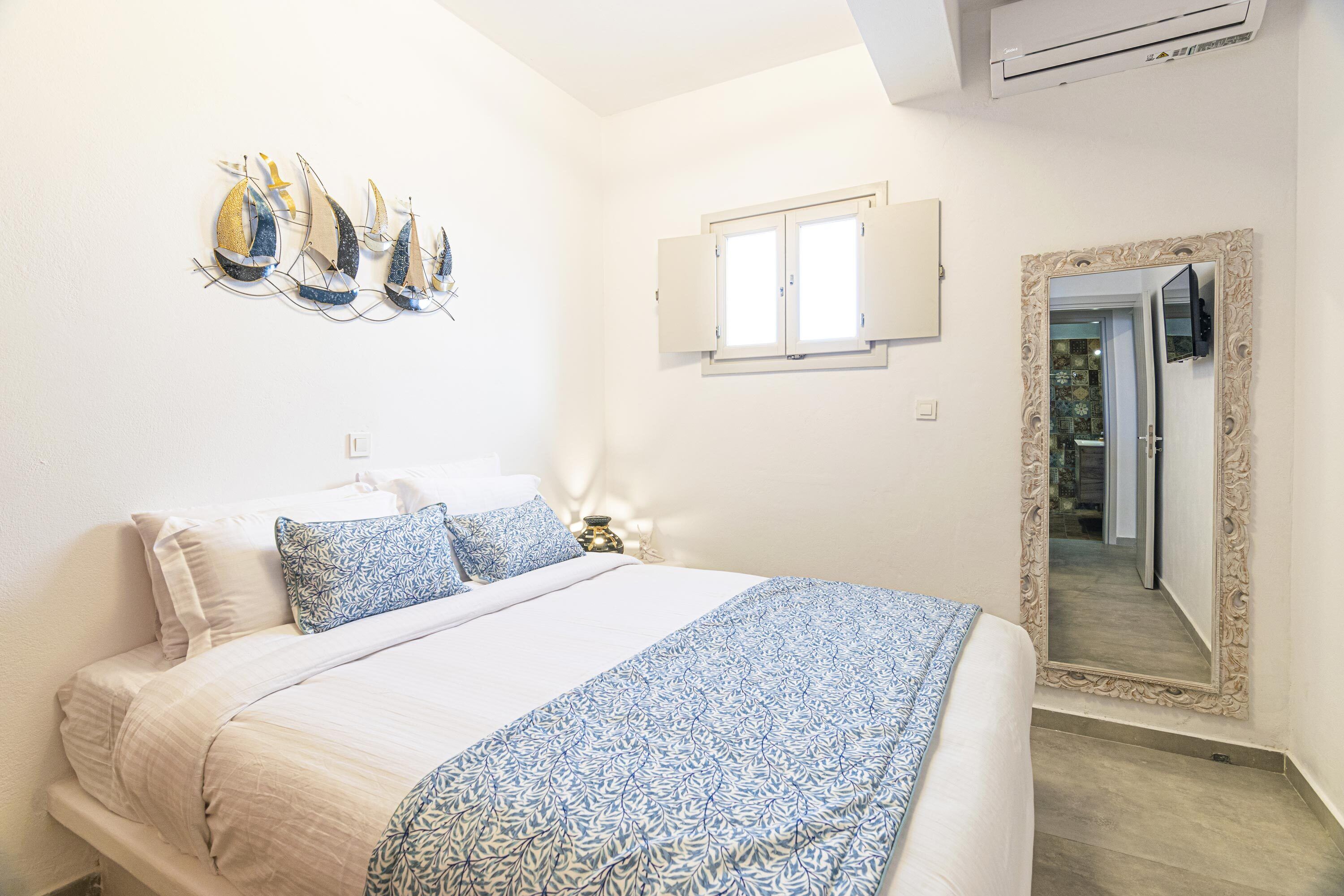 Um quarto com cama, janela, espelho e um enfeite na parede.