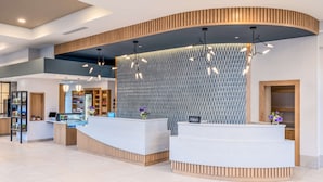 Uma área de recepção moderna de hotel, com um balcão curvo, parede estampada e iluminação pendente.