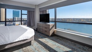 Quarto de hotel com uma cama grande, uma televisão em uma cômoda de madeira e vista para a cidade e o rio.