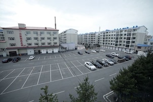 Um estacionamento com vários carros e um edifício com uma placa vermelha.