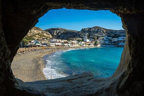 Vista costeira através de uma abertura de caverna, com uma praia, águas azul-claras e edifícios numa encosta.