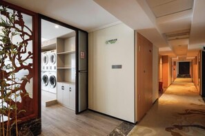Corredor de hotel com lavanderia, área de recepção e piso coberto de carpete.