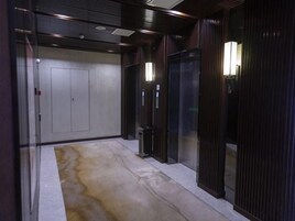 Corredor com piso molhado, dois elevadores e uma porta com câmera de segurança.