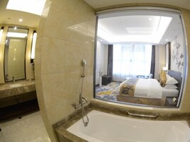 Quarto de hotel com um espelho grande, banheira, cama com cabeceira e janela com cortinas.