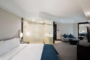 Quarto de hotel moderno com uma cama grande, um sofá, uma escrivaninha e um separador de vidro.
