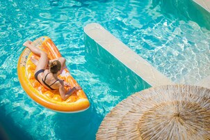 Uma pessoa boiando em um flutuador laranja em uma piscina azul cristalina.