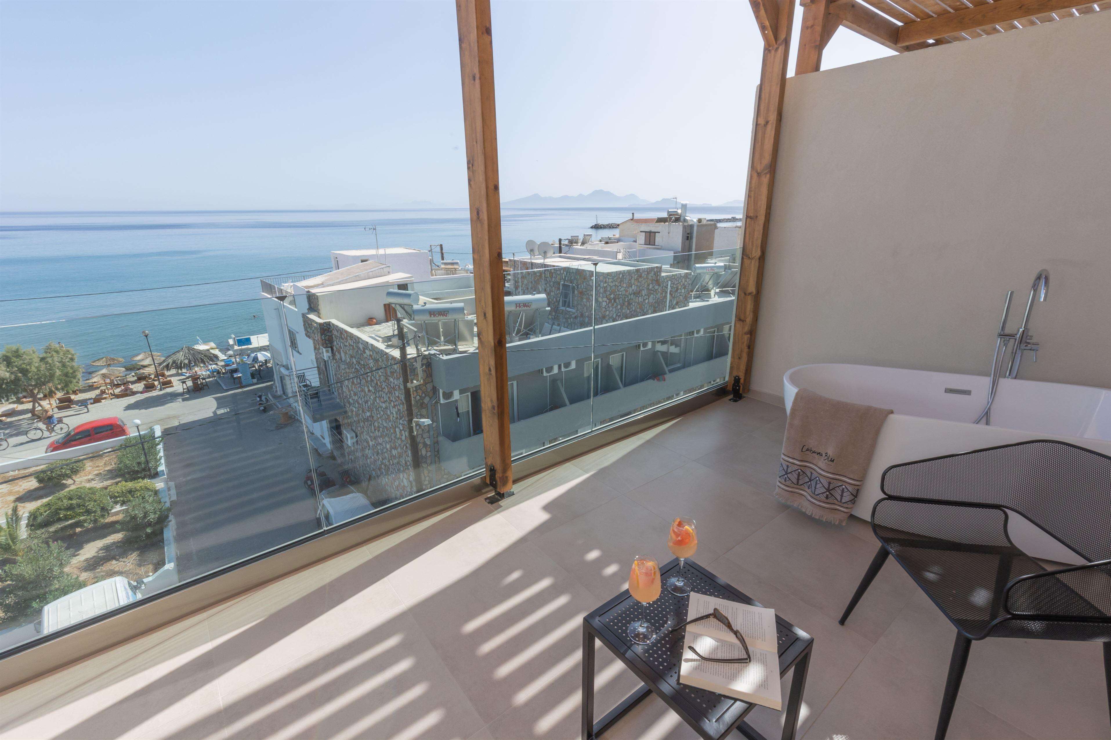 Varanda com vista para o mar, um sofá, uma mesa com bebidas e uma toalha.