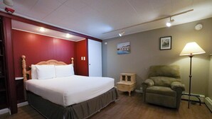 Quarto de hotel com cama, uma cadeira, mesa de cabeceira e luminária.