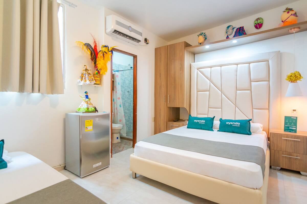 Quarto de hotel com cama, guarda-roupa, secretária e ar condicionado.