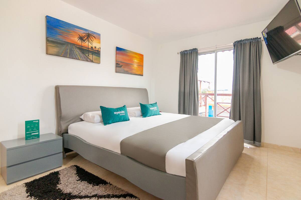 Quarto moderno com cama, mesas de cabeceira, televisão de tela plana e obras de arte nas paredes.