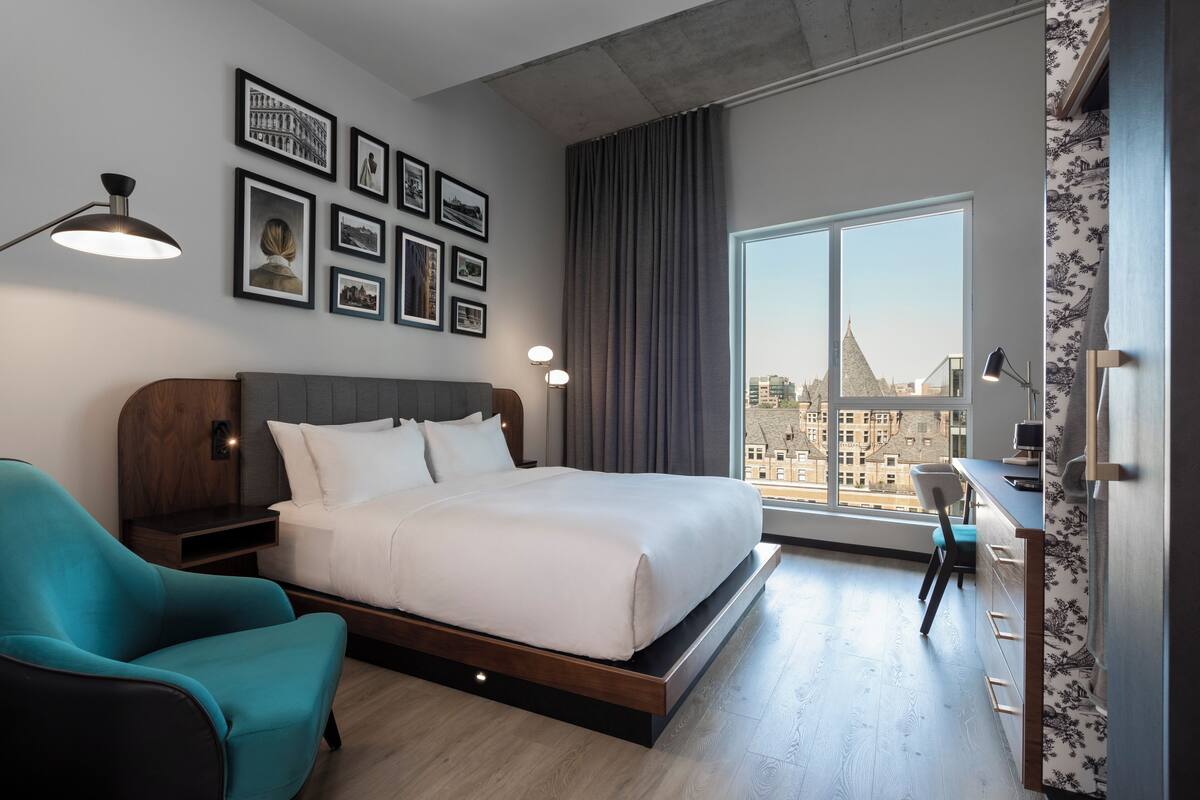 Quarto de hotel moderno com uma cama grande, uma escrivaninha e vista para a cidade.