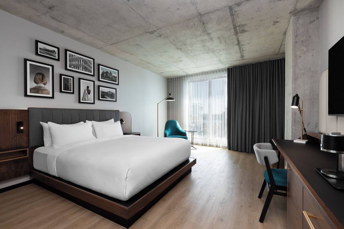 Quarto de hotel moderno com uma cama grande, uma escrivaninha, uma cadeira e uma televisão.