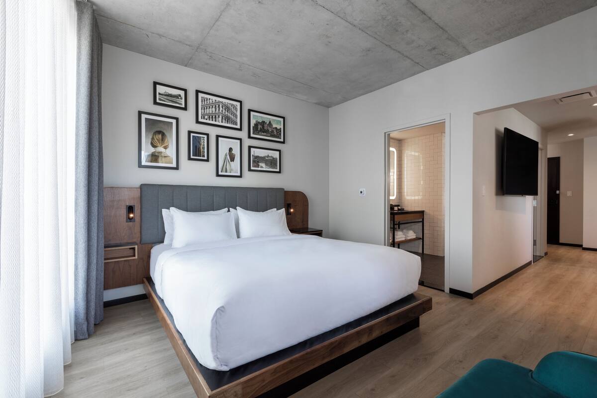 Quarto de hotel moderno com uma cama grande, cabeceira de madeira e televisão de tela plana na parede.