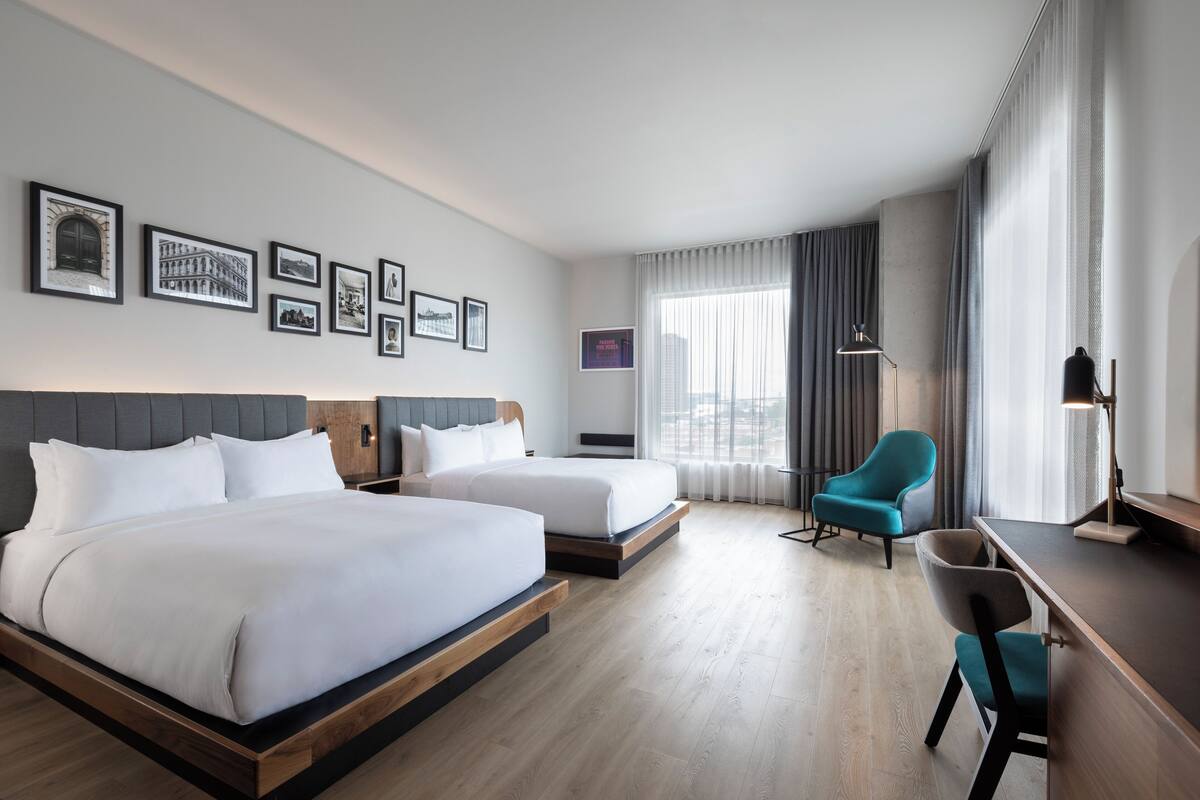 Quarto de hotel moderno com duas camas, uma escrivaninha, uma cadeira e quadros nas paredes.