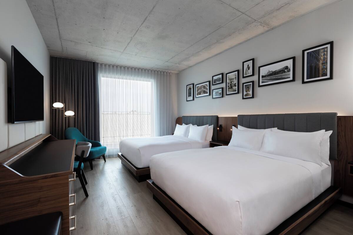 Quarto de hotel com duas camas, uma escrivaninha, uma cadeira e uma televisão.