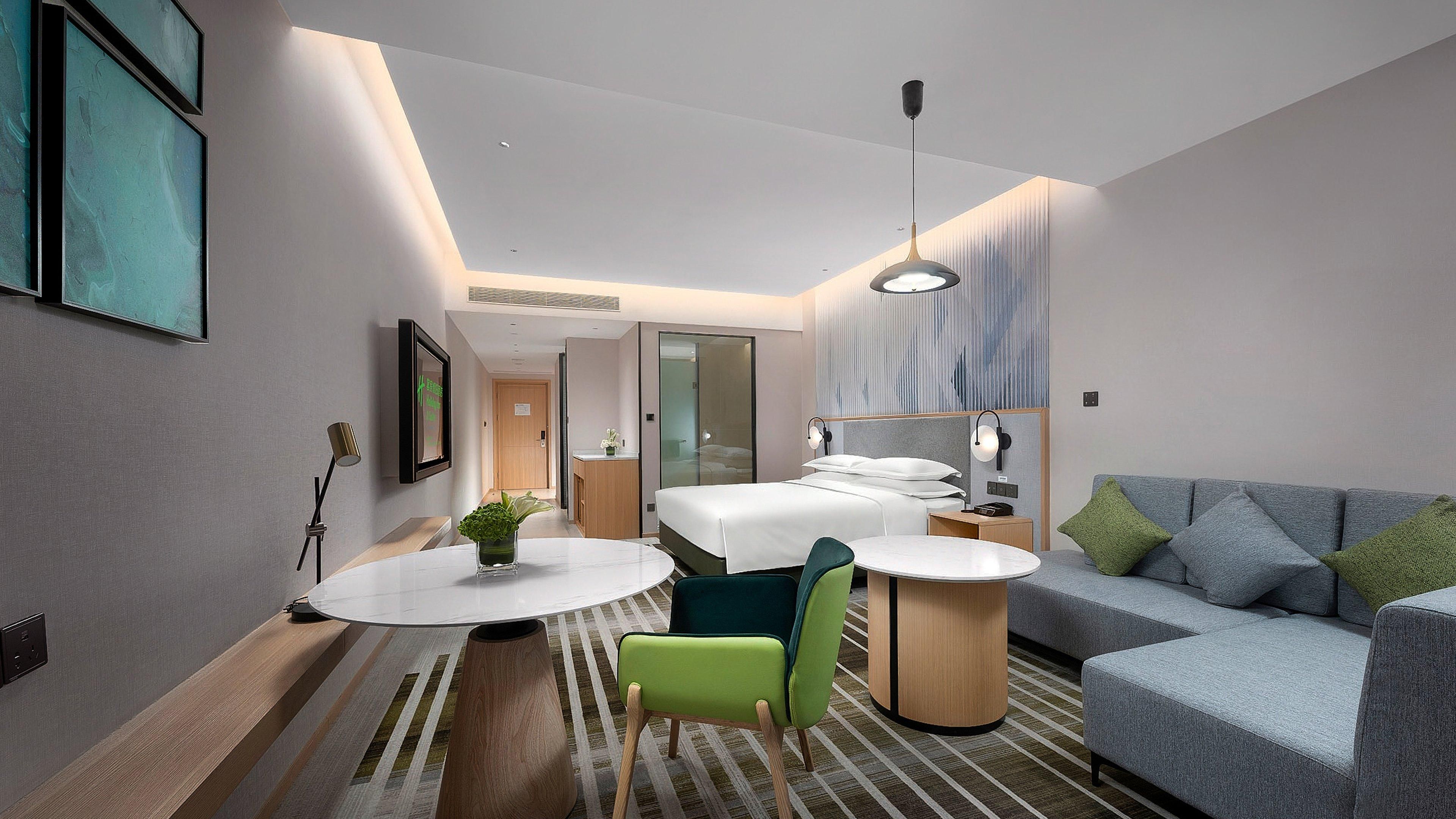 Quarto de hotel moderno com cama, sofá, mesa de jantar e uma pequena cadeira verde.