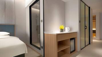 Quarto de hotel moderno com uma cama, uma toucador de madeira com espelho, uma pia pequena e área de chuveiro.