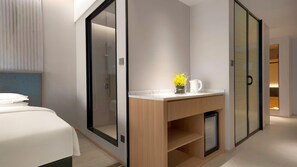 Quarto de hotel moderno com uma cama, uma toucador de madeira com espelho, uma pia pequena e área de chuveiro.
