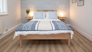 Um quarto com cama de madeira, roupa de cama estampada, duas mesas de cabeceira com abajures, uma parede com design texturizado e quadros na parede.