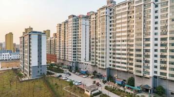 Um edifício residencial alto, com vários andares, varandas e um estacionamento em frente.