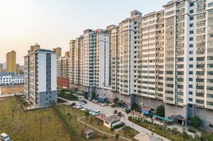 Um edifício residencial alto, com vários andares, varandas e um estacionamento em frente.
