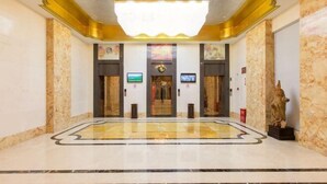 Um hall amplo com piso de mármore, um lustre central e uma estátua à direita.