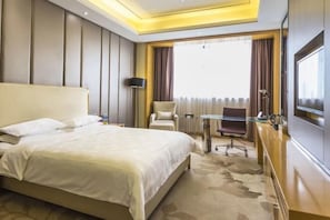 Quarto de hotel com uma cama grande, uma escrivaninha com cadeira, televisão e janela com cortinas.